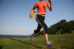 Joggende Frau mit Trinkflasche auf einer Wiese